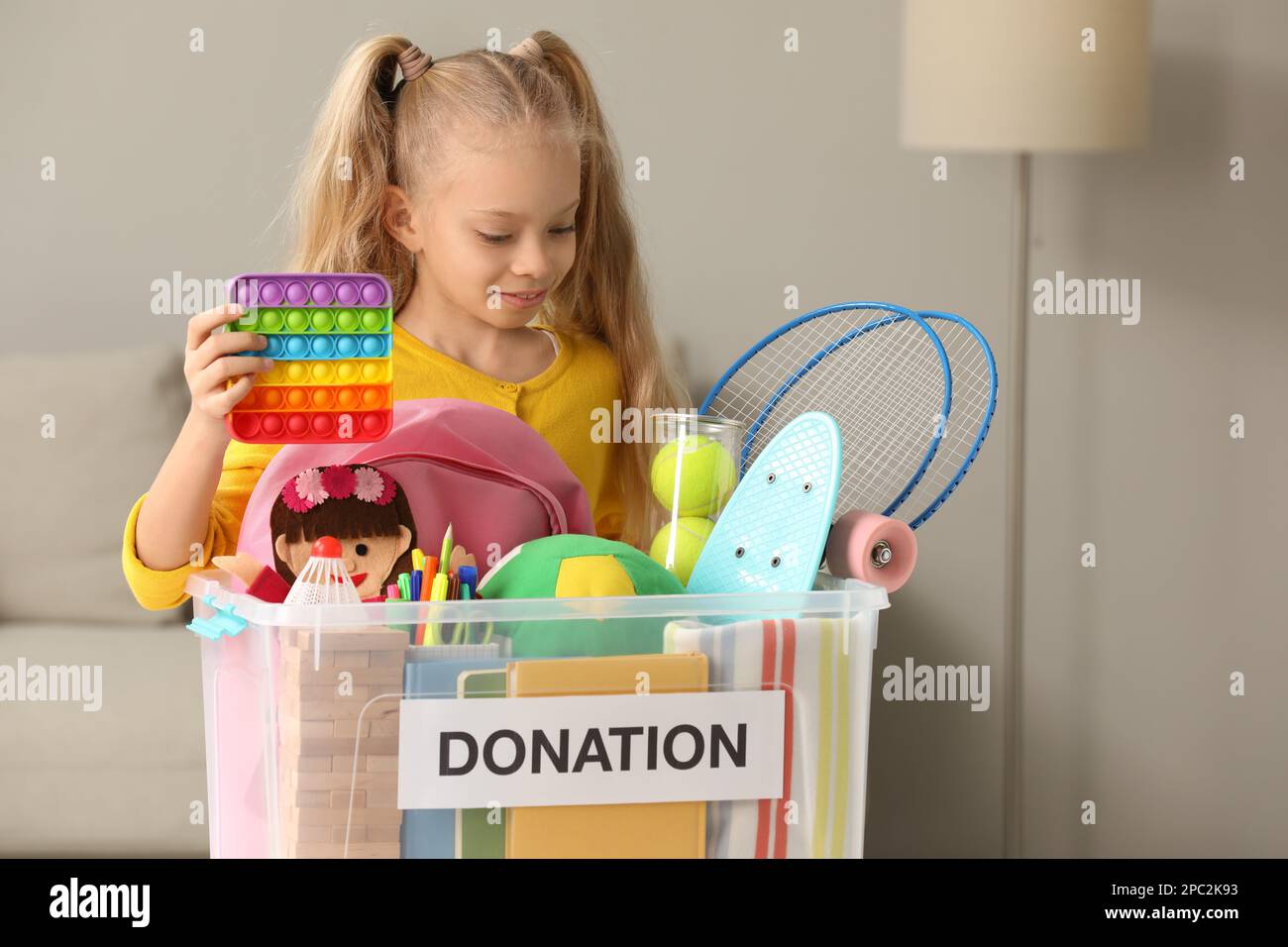 Cute little girl putting toy into donation box at home, space for text ...