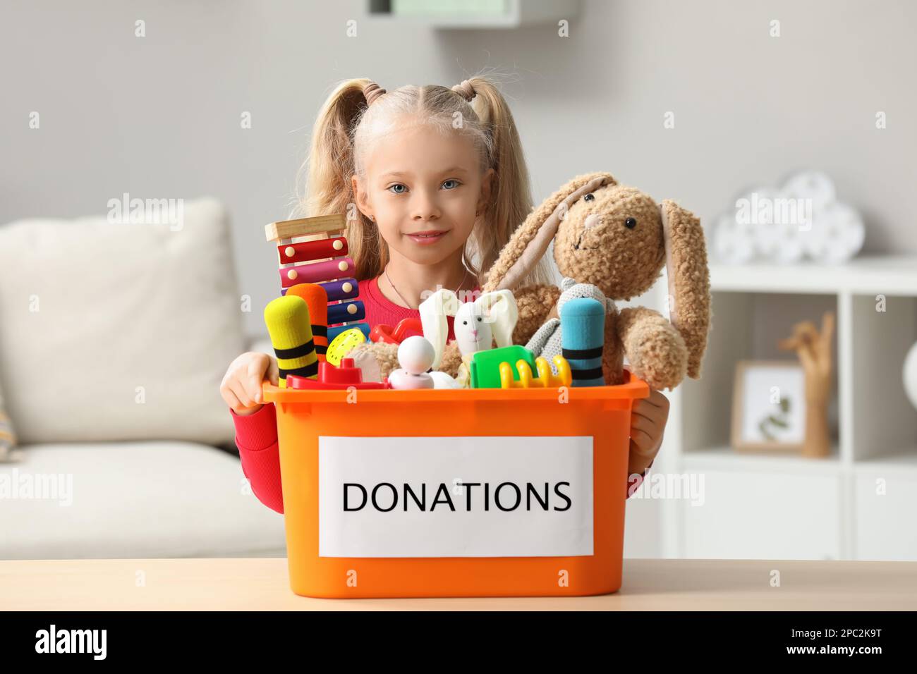 Cute little girl holding donation box with toys at home Stock Photo - Alamy