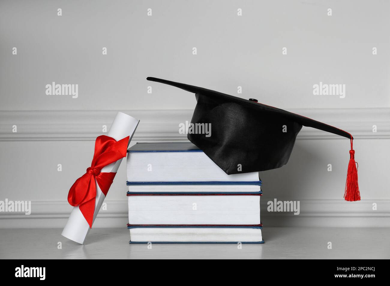 Graduation hat, books and diploma on floor near white wall Stock Photo ...