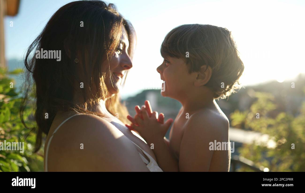 Joyful mother holding baby child son in arms during beautiful sunset time. Parent bonding with ...