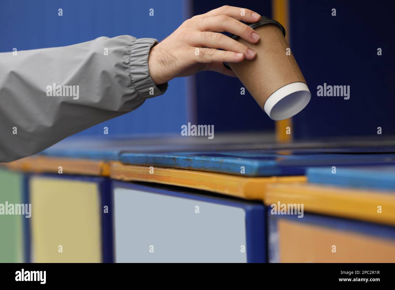 Man throwing paper coffee cup into garbage bin outdoors, closeup. Waste ...