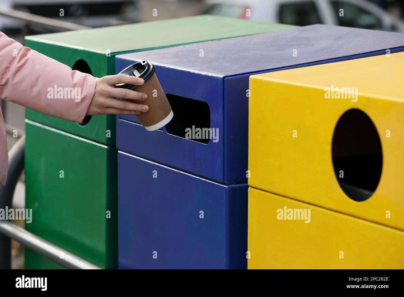 Woman throwing paper coffee cup into garbage bin outdoors, closeup ...