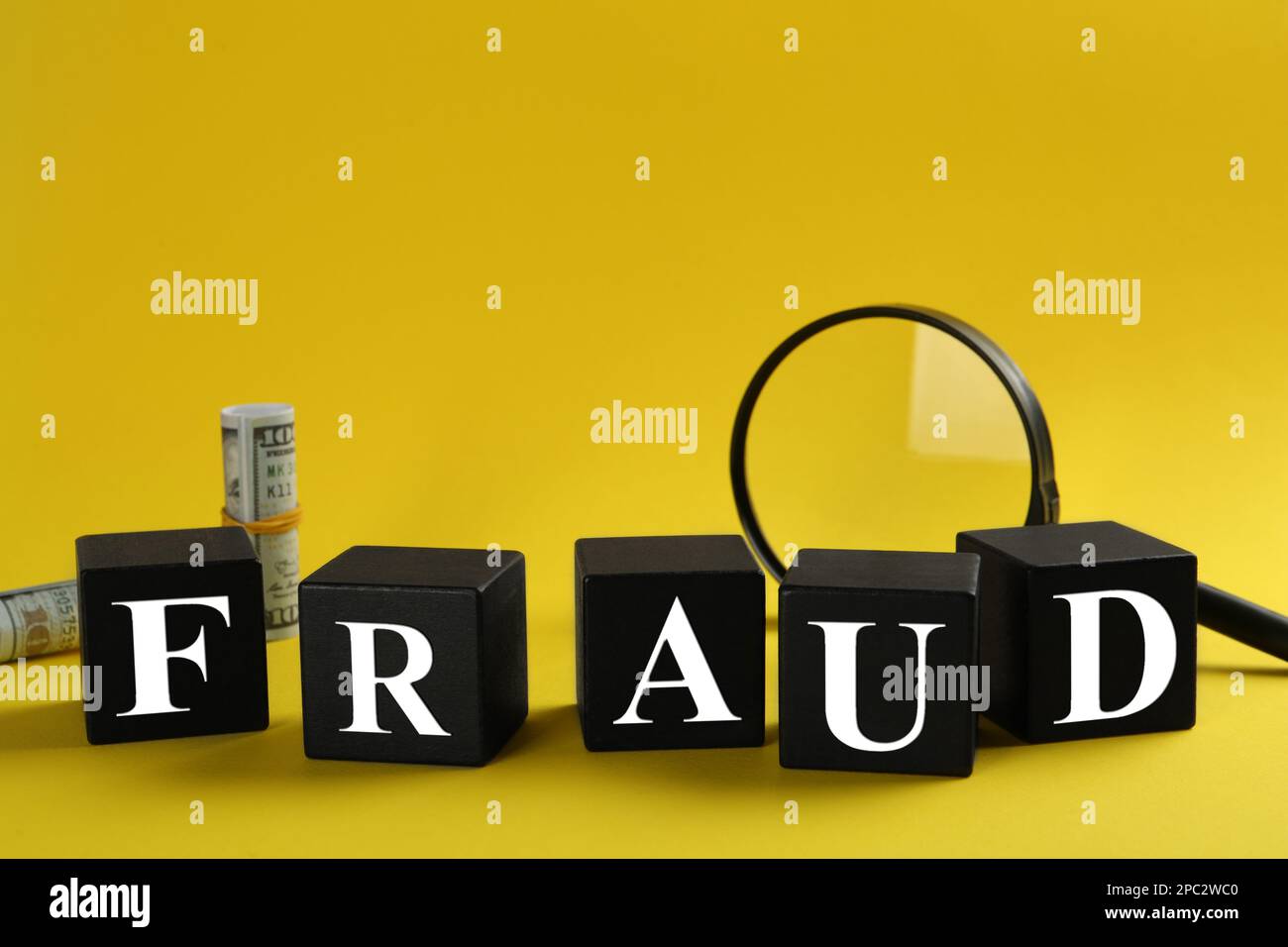 Black cubes with word Fraud, magnifying glass and money on yellow ...