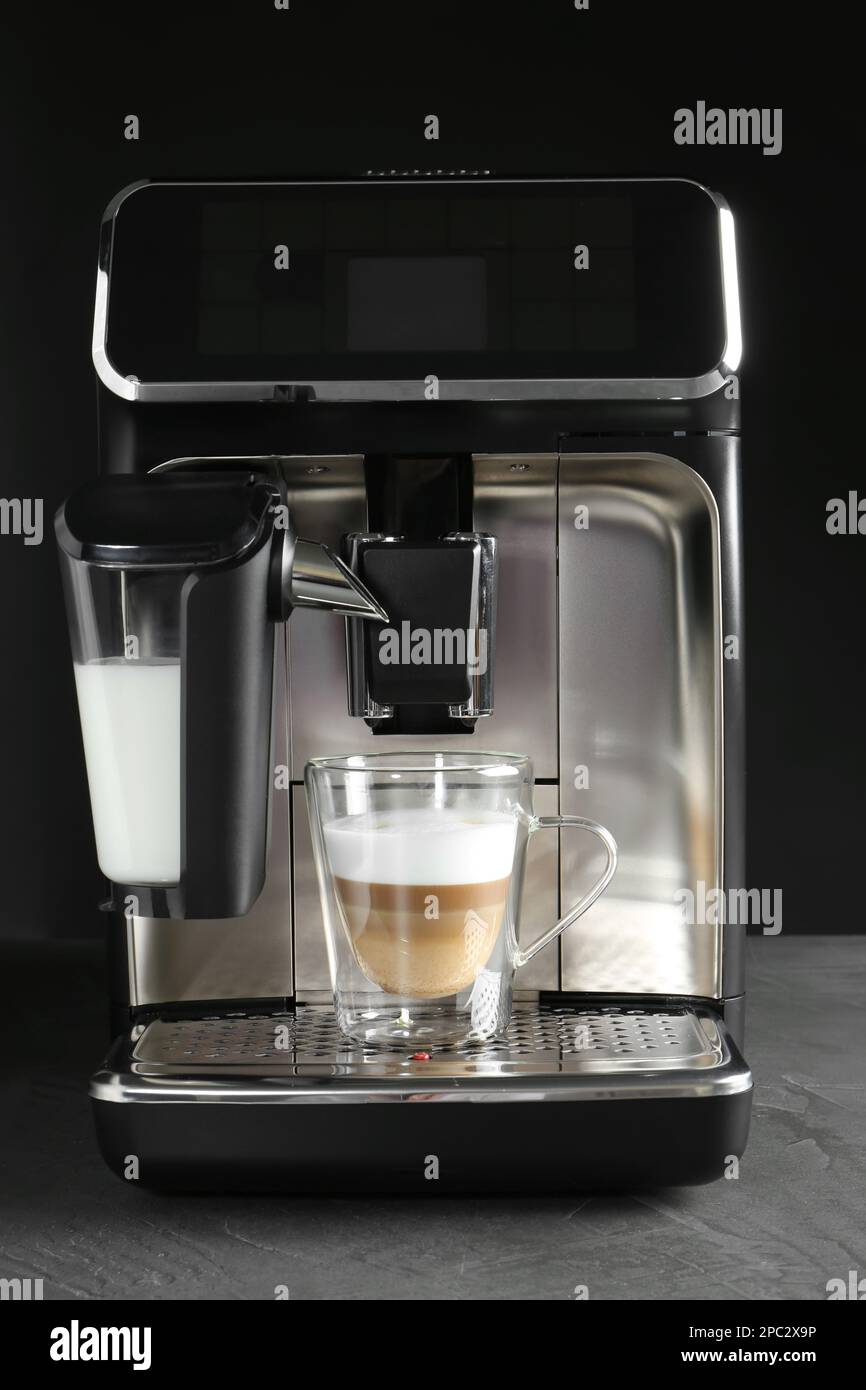 Modern coffee machine with glass cup of latte on grey table against ...