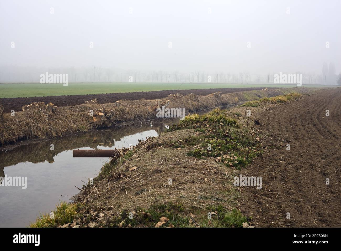 Drainage channel and a stream of water between fields on a foggy day in ...