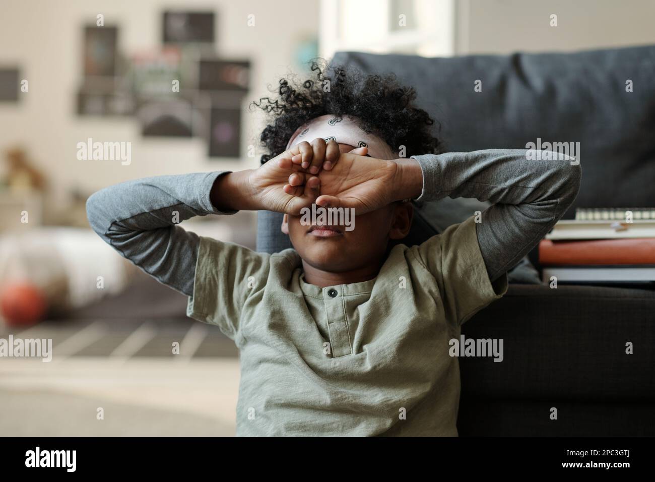 Offended or tired African American boy in grey pajamas hiding his face ...