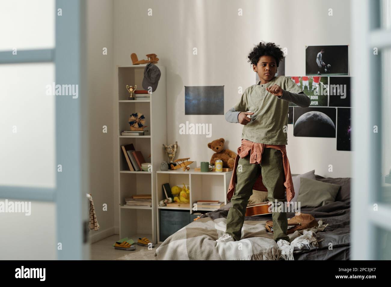 Cute active schoolboy standing on double bed and training defense ...