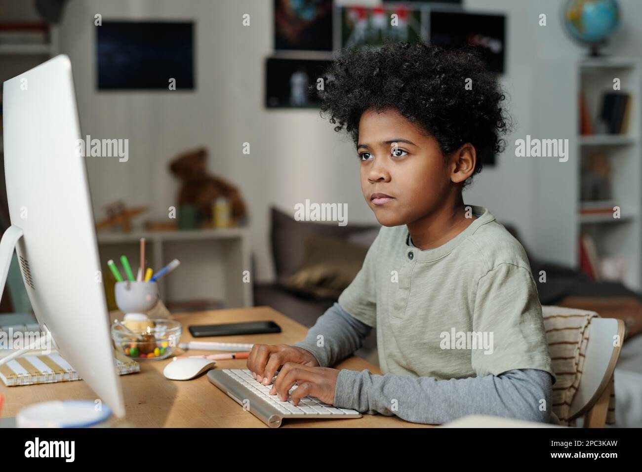 Serious schoolboy sitting in front of computer screen in living room ...