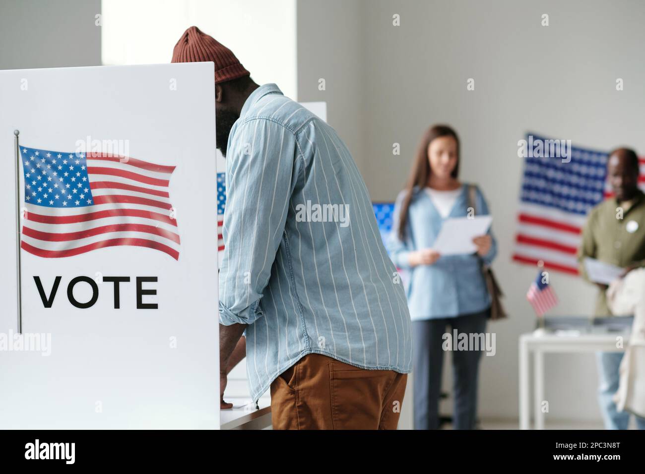 Side view of young African American male voter filling in ballot while ...