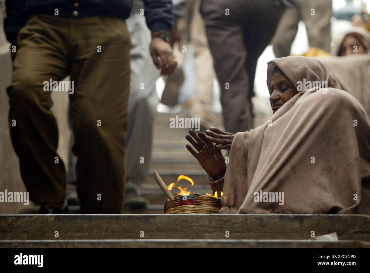 A homeless Indian woman warms her hands by making a fire at a bus ...