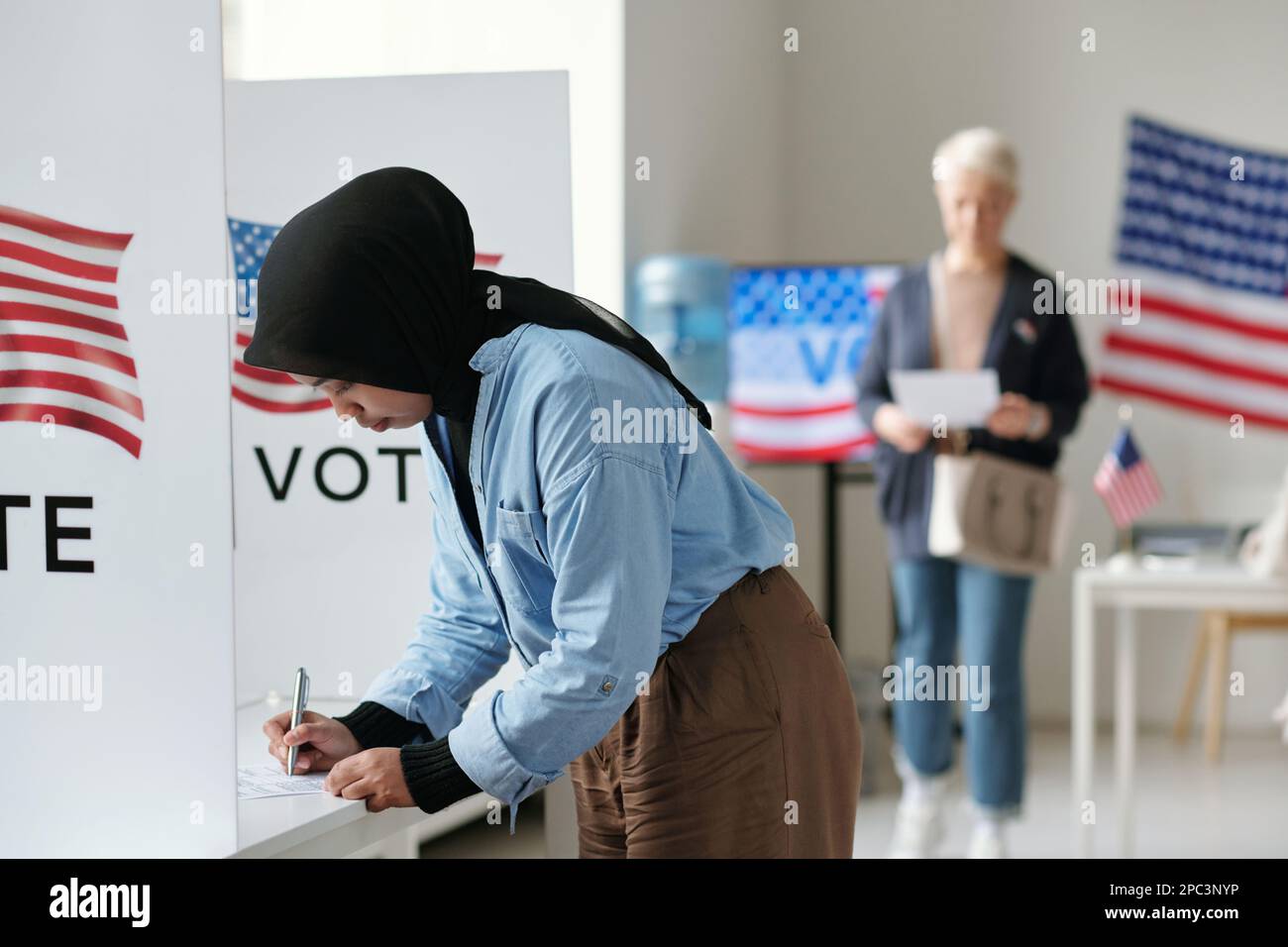 Young Muslim woman in hijab bending over vote booth and making her ...