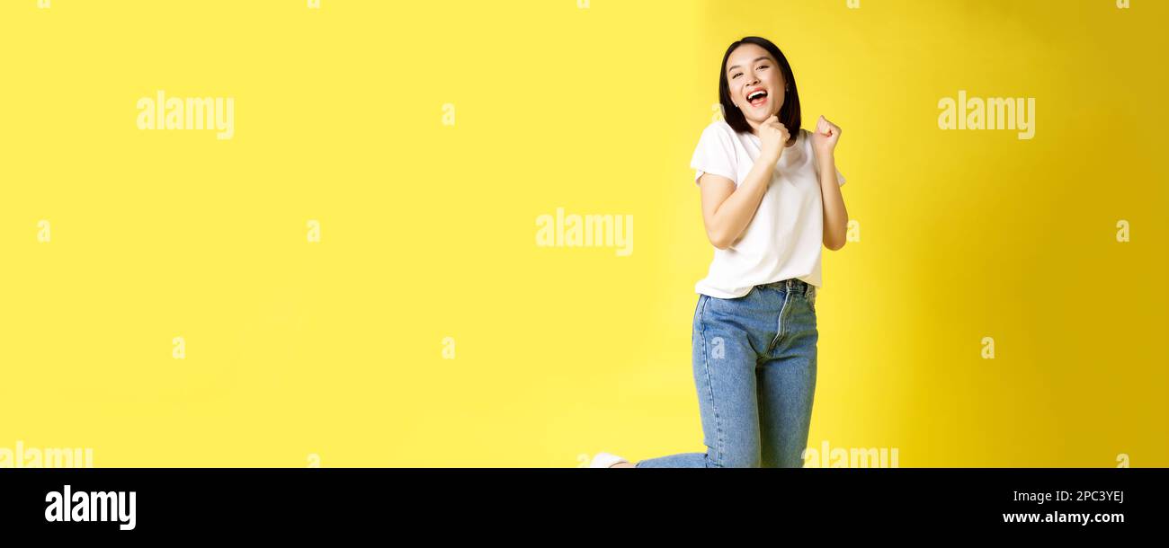 Full size shot of happy asian woman dancing and jumping from happiness ...