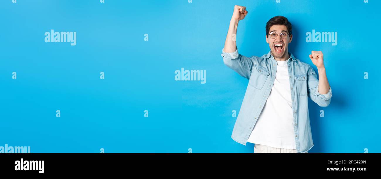 Excited handsome man triumphing, raising hands up and shouting for joy ...