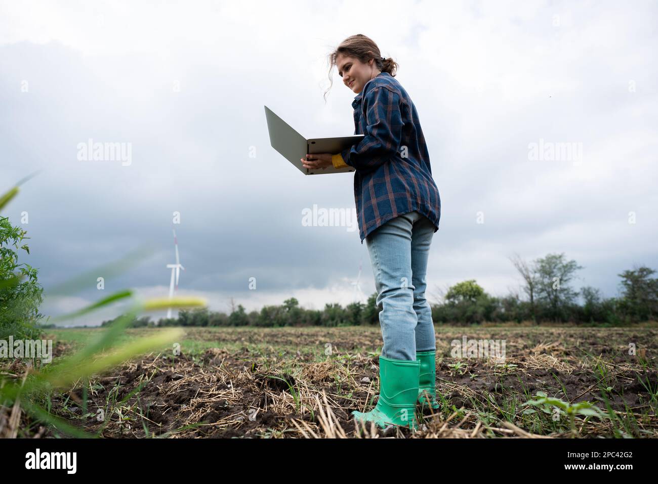 Farmer with laptop on the field. Wind turbines on a horizon. Smart ...