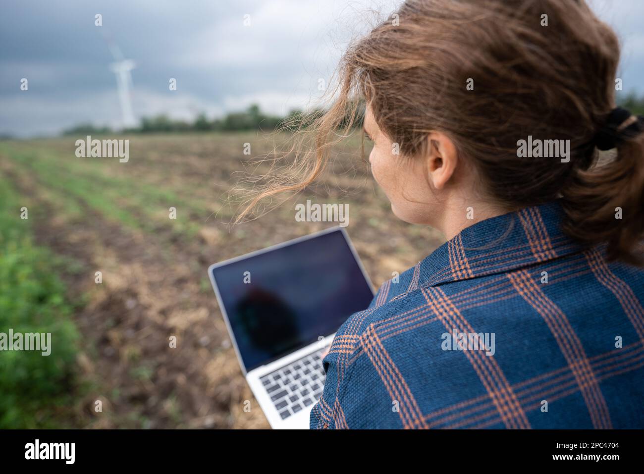 Farmer with laptop on the field. Wind turbines on a horizon. Smart ...