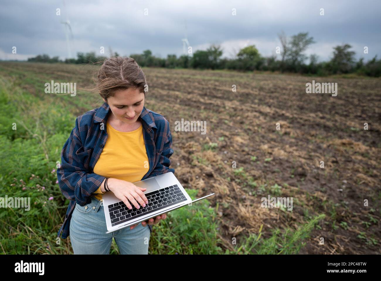 Farmer with laptop on the field. Wind turbines on a horizon. Smart ...