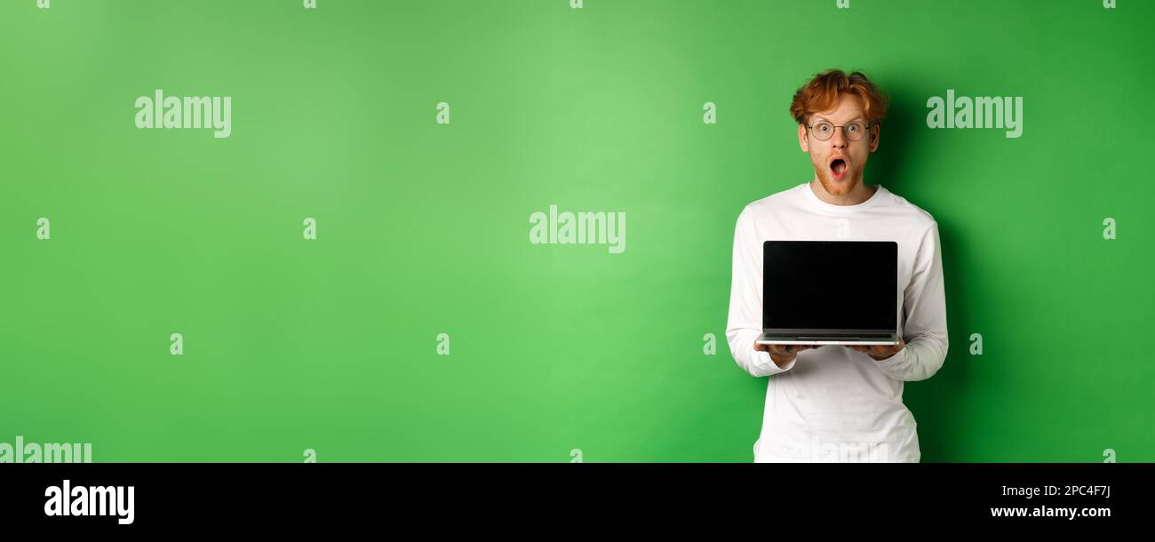 Surprised redhead man in glasses showing laptop blank screen, showing ...