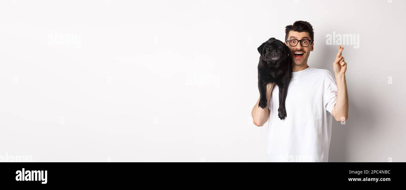 Hopeful smiling dog owner making a wish, holding cute black pug on ...