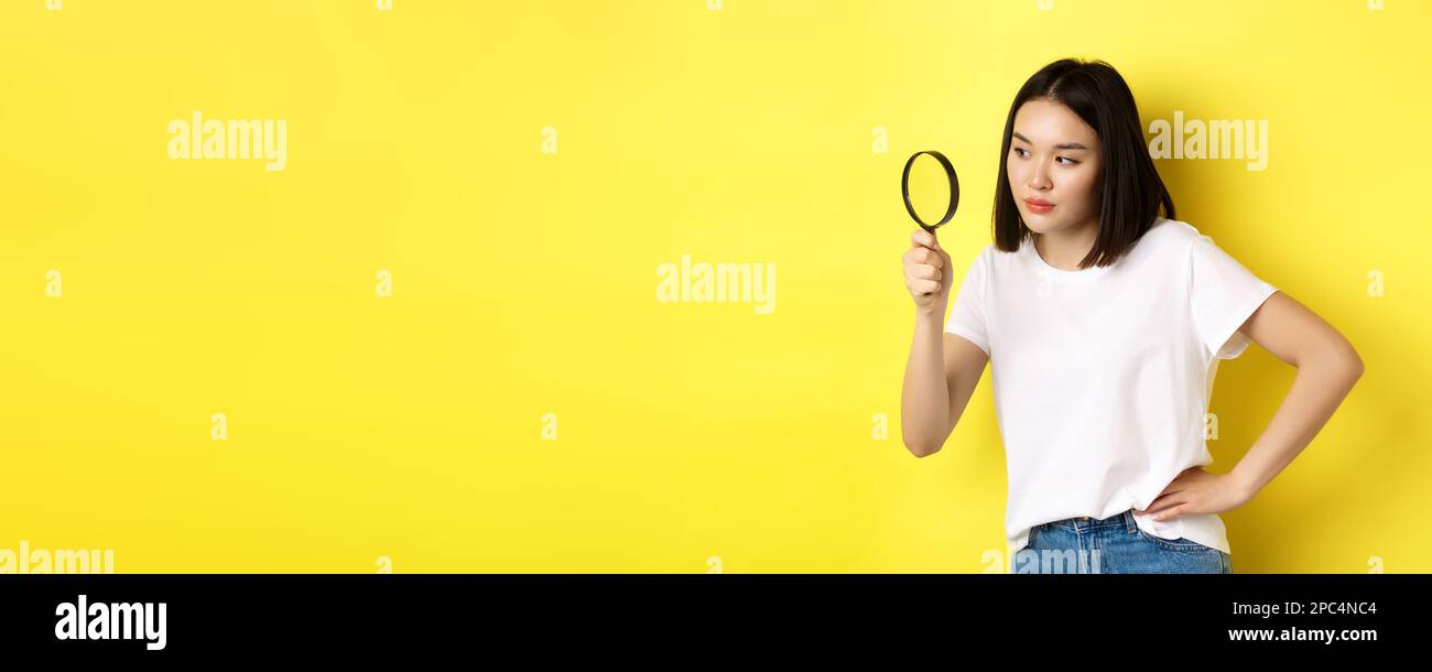 Asian woman detective looking through magnifying glass with intrigued ...