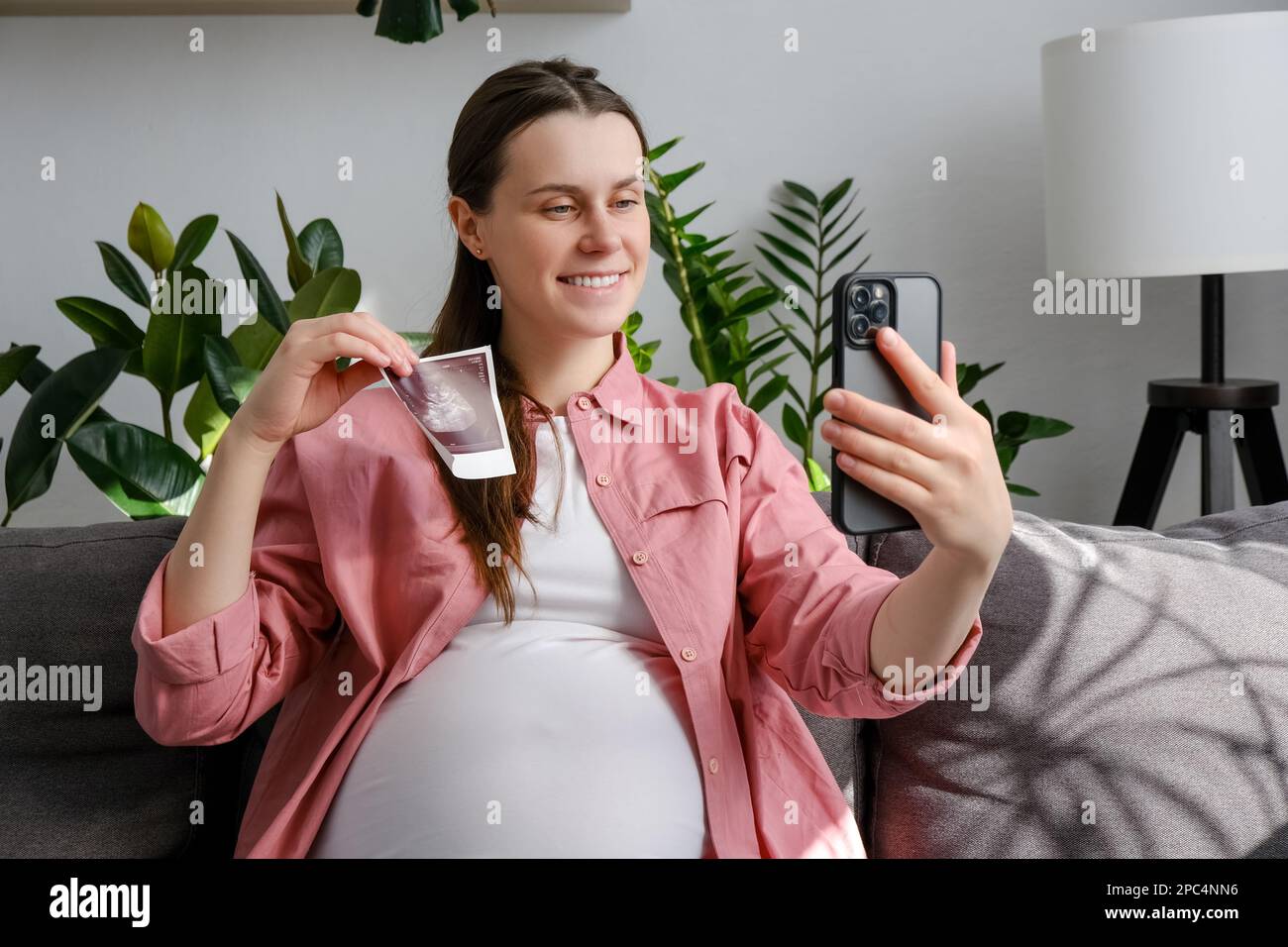 Attractive smiling young pregnant woman sitting on comfy couch showing ...