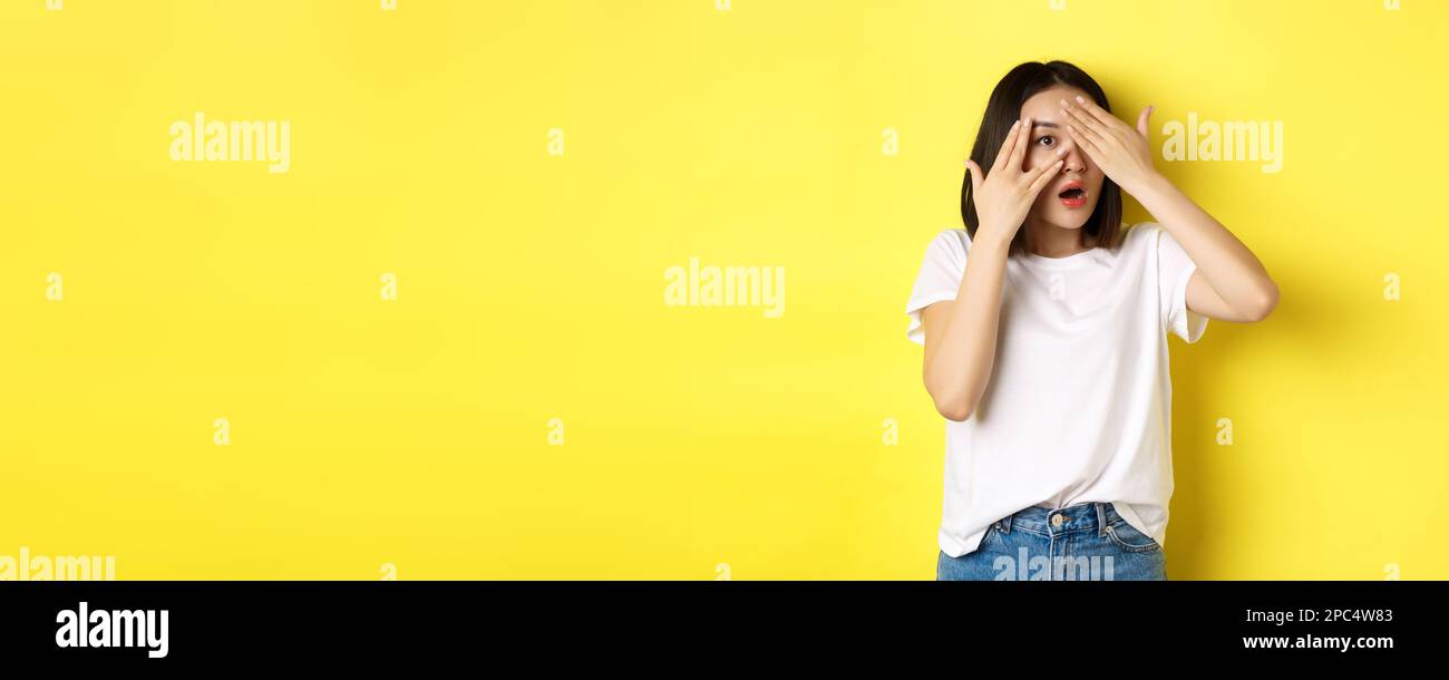 Intrigued asian girl waiting for surprise, peeking through fingers on ...