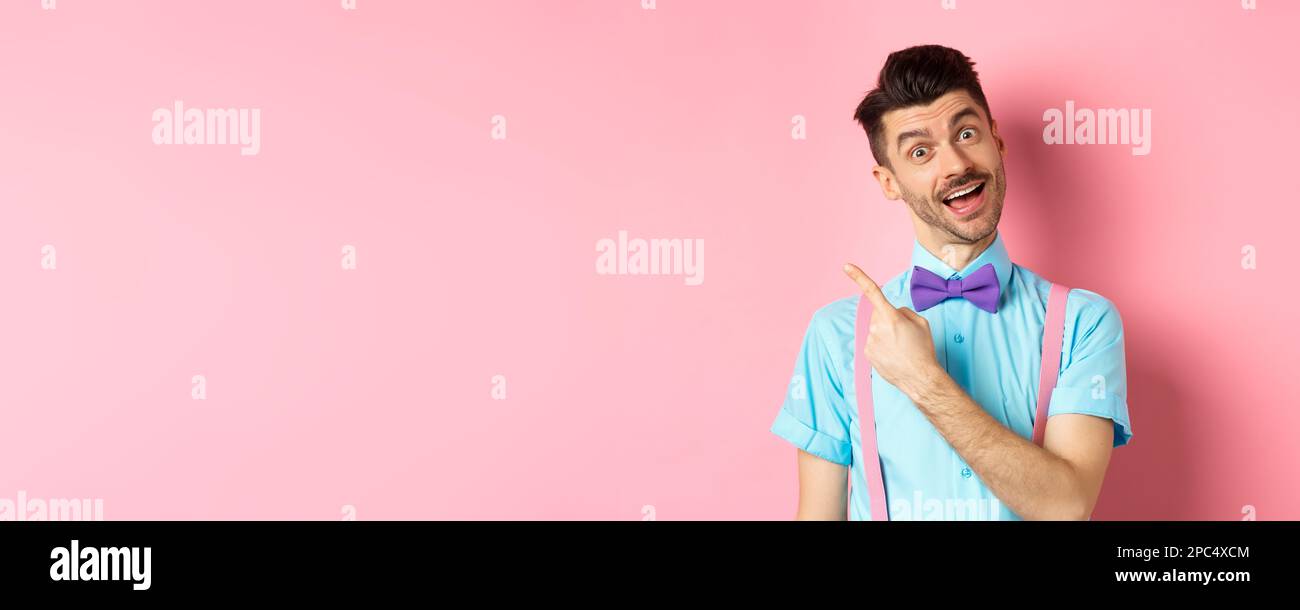 Funny male model in bow-tie, tilt head and pointing finger left ...