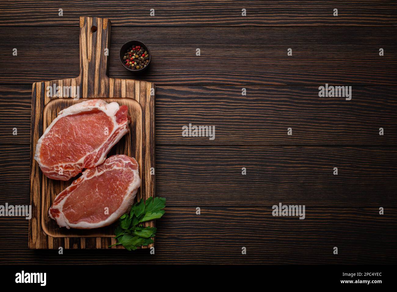 Cut raw meat pork steaks with seasonings on kitchen cutting board ...
