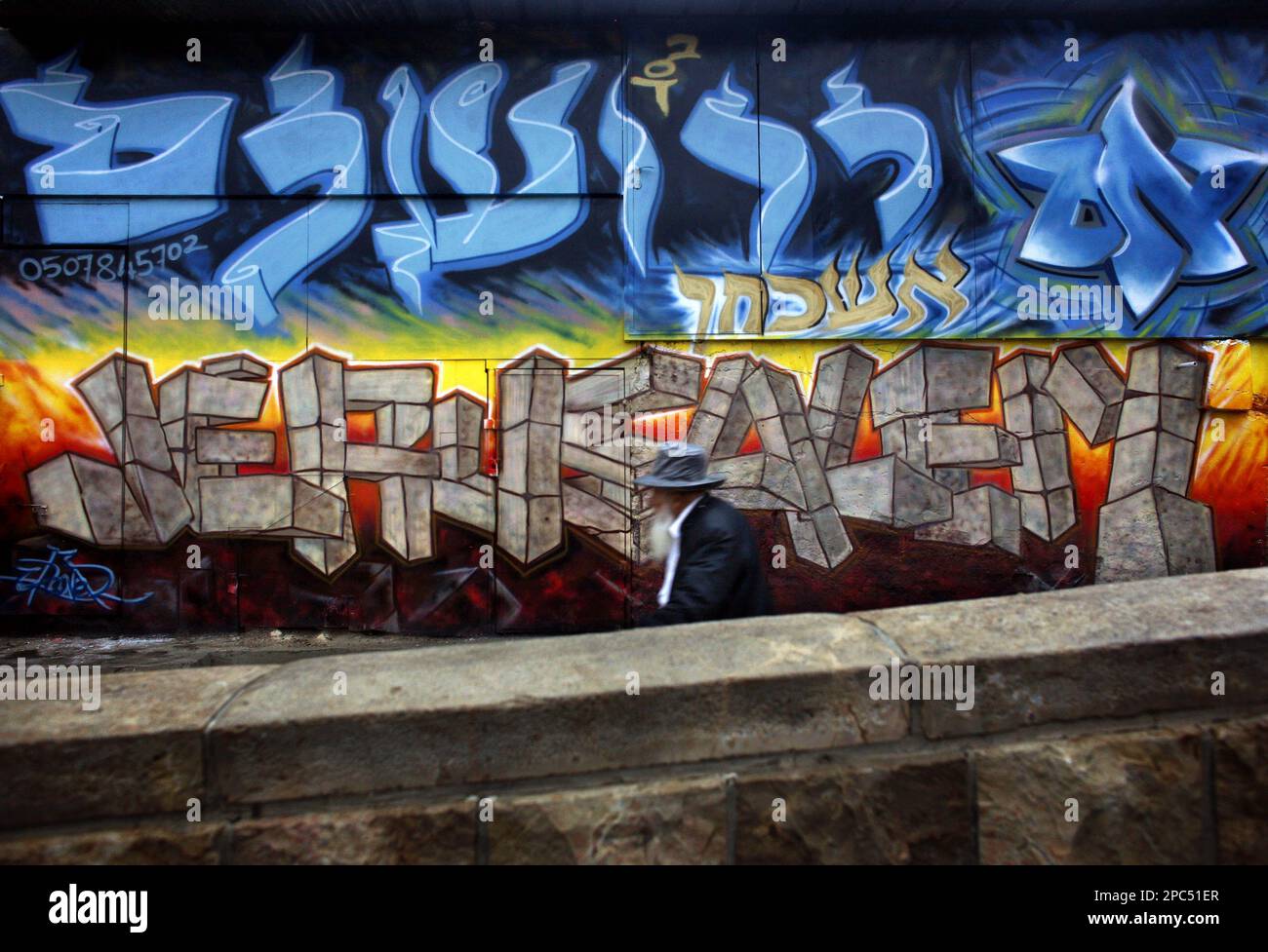 An Israeli man walks past a graffiti mural, with the words "Jerusalem ...