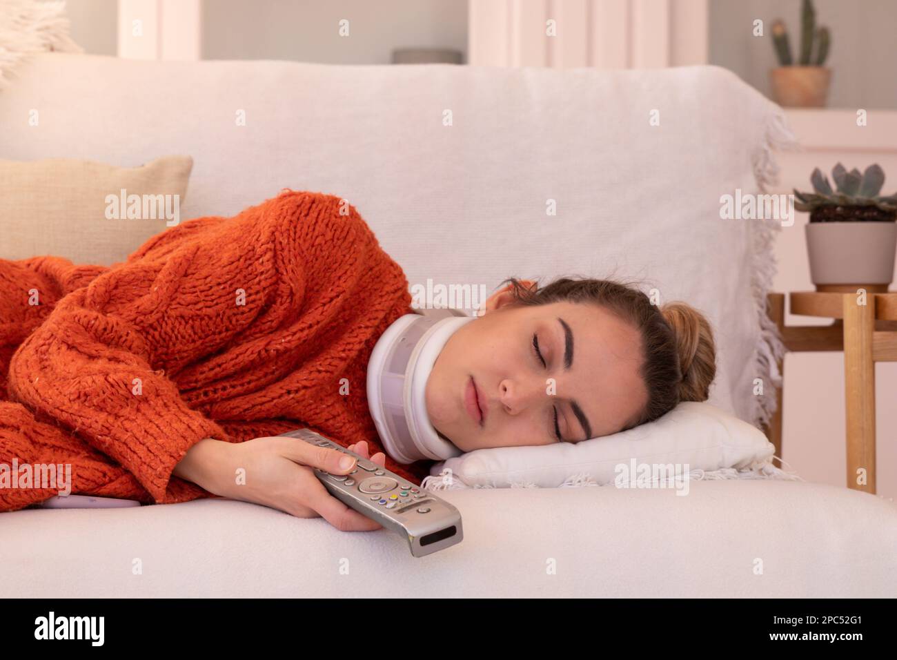 Young woman in orange sweater wearing orthopedic collar holding TV ...