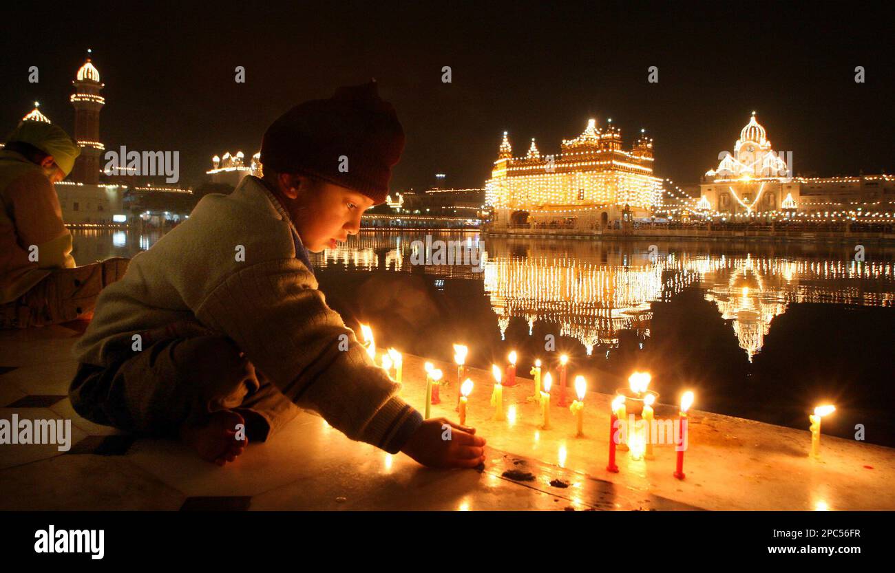 A Sikh devotee lights a candle before the illuminated Golden Temple ...