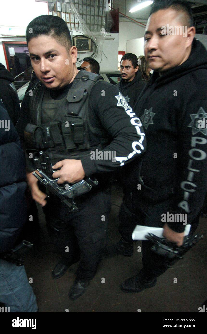 Two Tijuana city policemen hold their pistols as the line up to hand ...