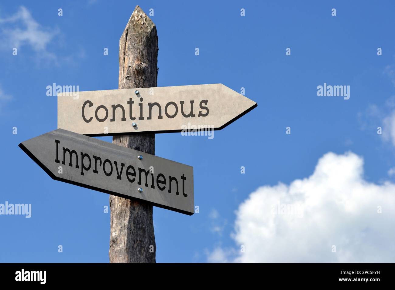 Continous improvement - wooden signpost with two arrows, sky with ...