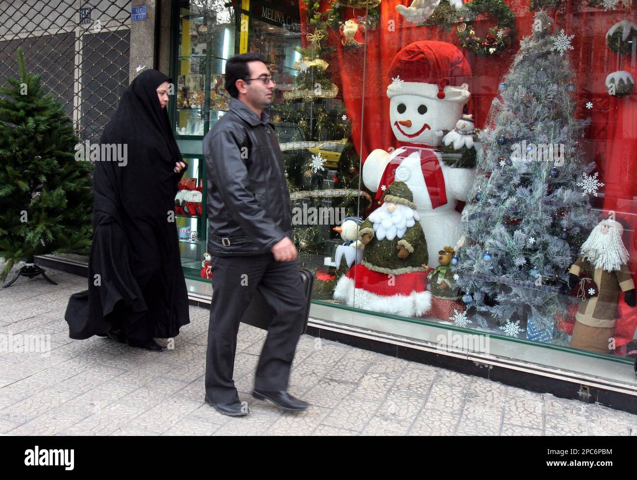 An Iranian Muslim couple walk past a shop decorate with images of Santa ...