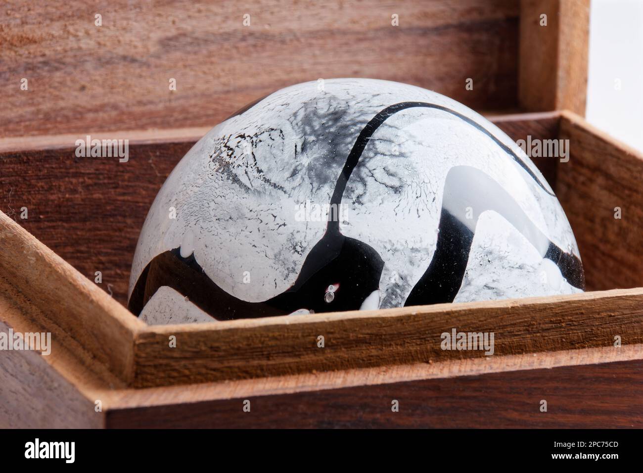 structured black and white glass sphere inside a wooden box isolated on ...
