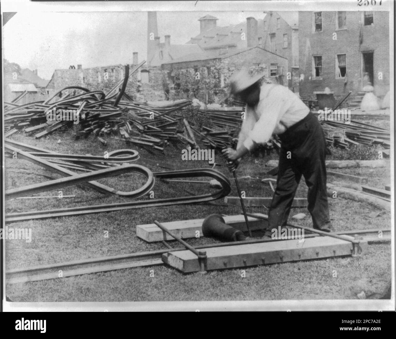 Railroad construction worker straightening track; pile of twisted rails ...