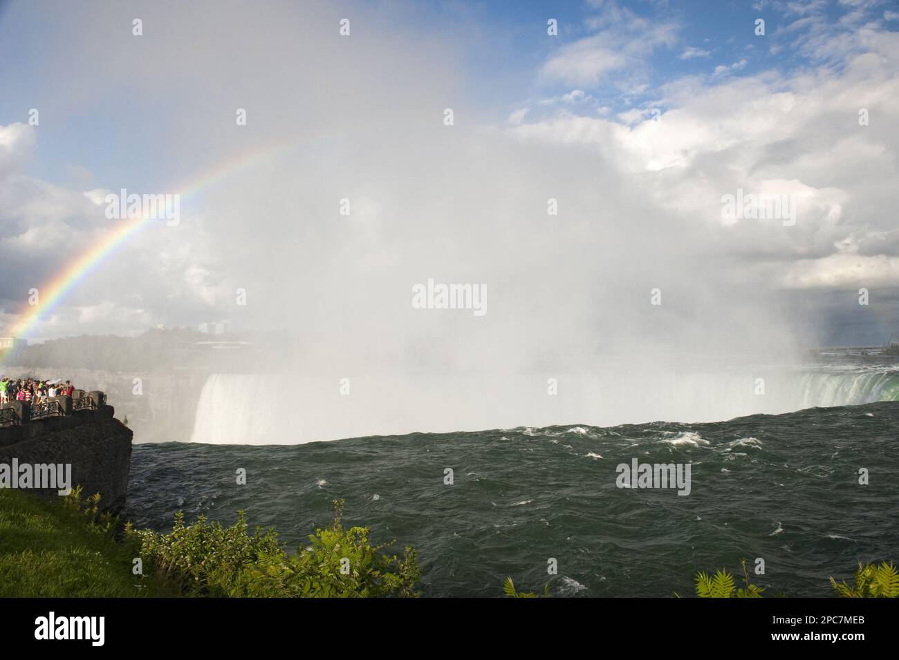 Rainbow forming in spray over waterfall, with tourists on viewing ...