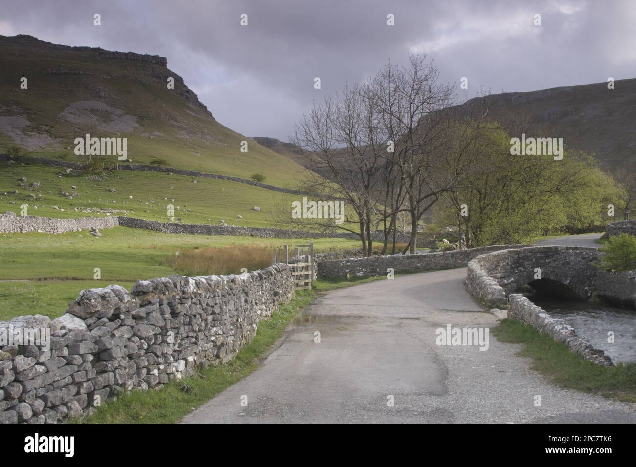 View of steep-sided valley, dry-stone walls, stone bridge, trees and ...