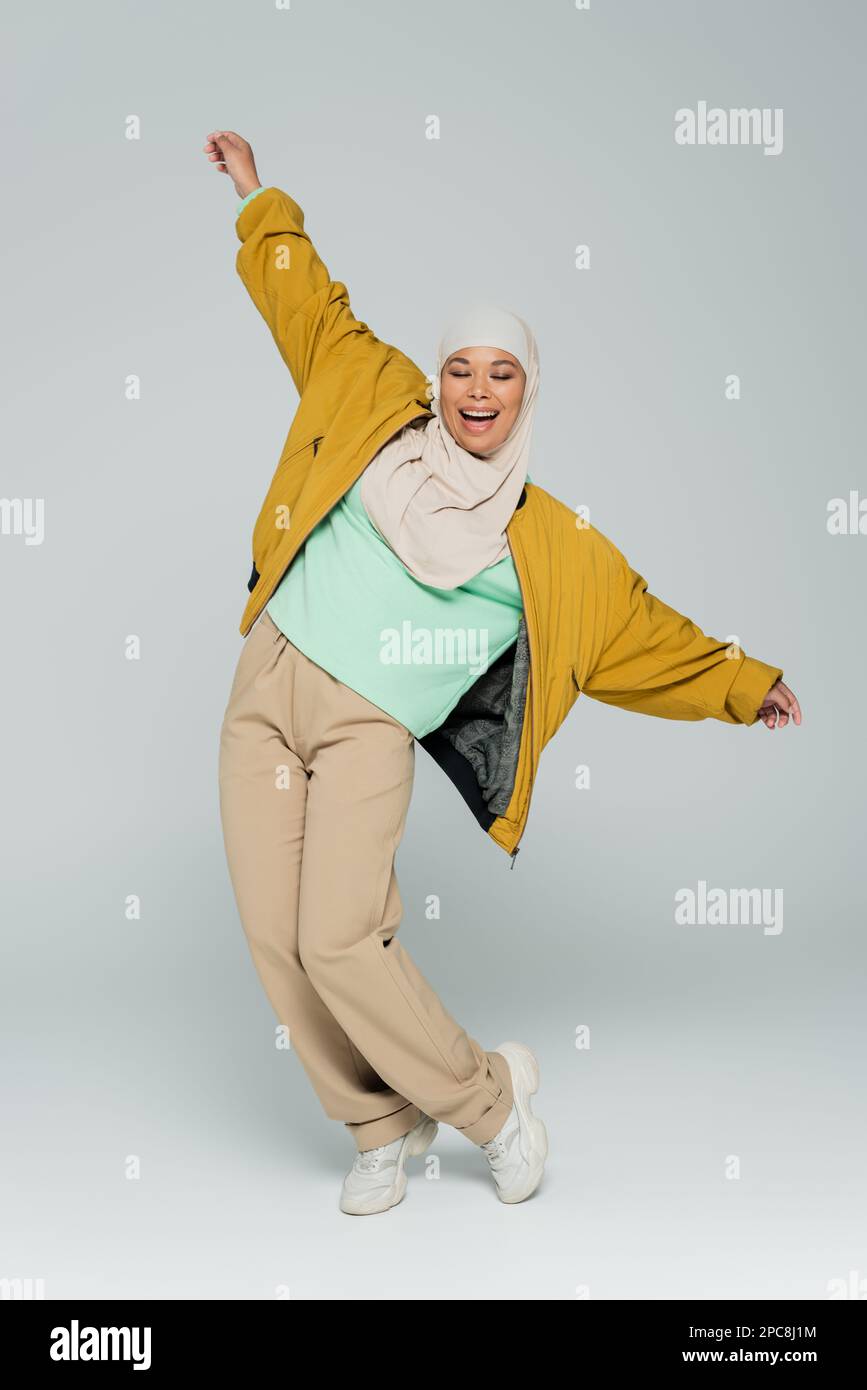full length of multiracial muslim woman in yellow bomber jacket and ...
