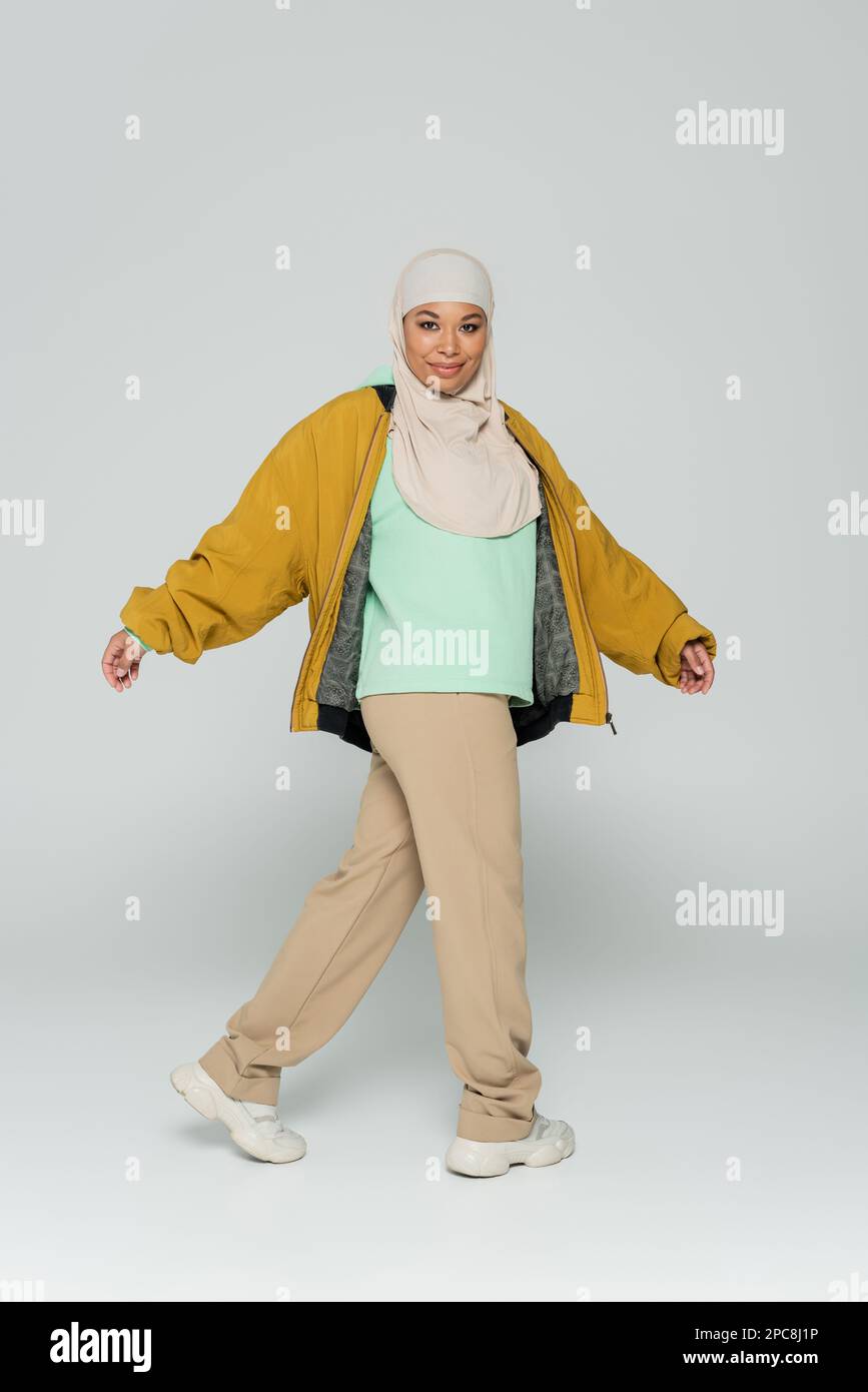 full length of cheerful multiracial muslim woman in yellow bomber ...
