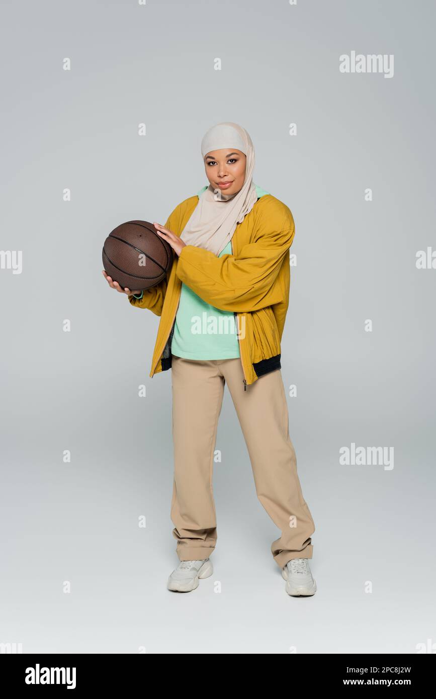 full length of stylish multiracial muslim woman in yellow bomber jacket ...