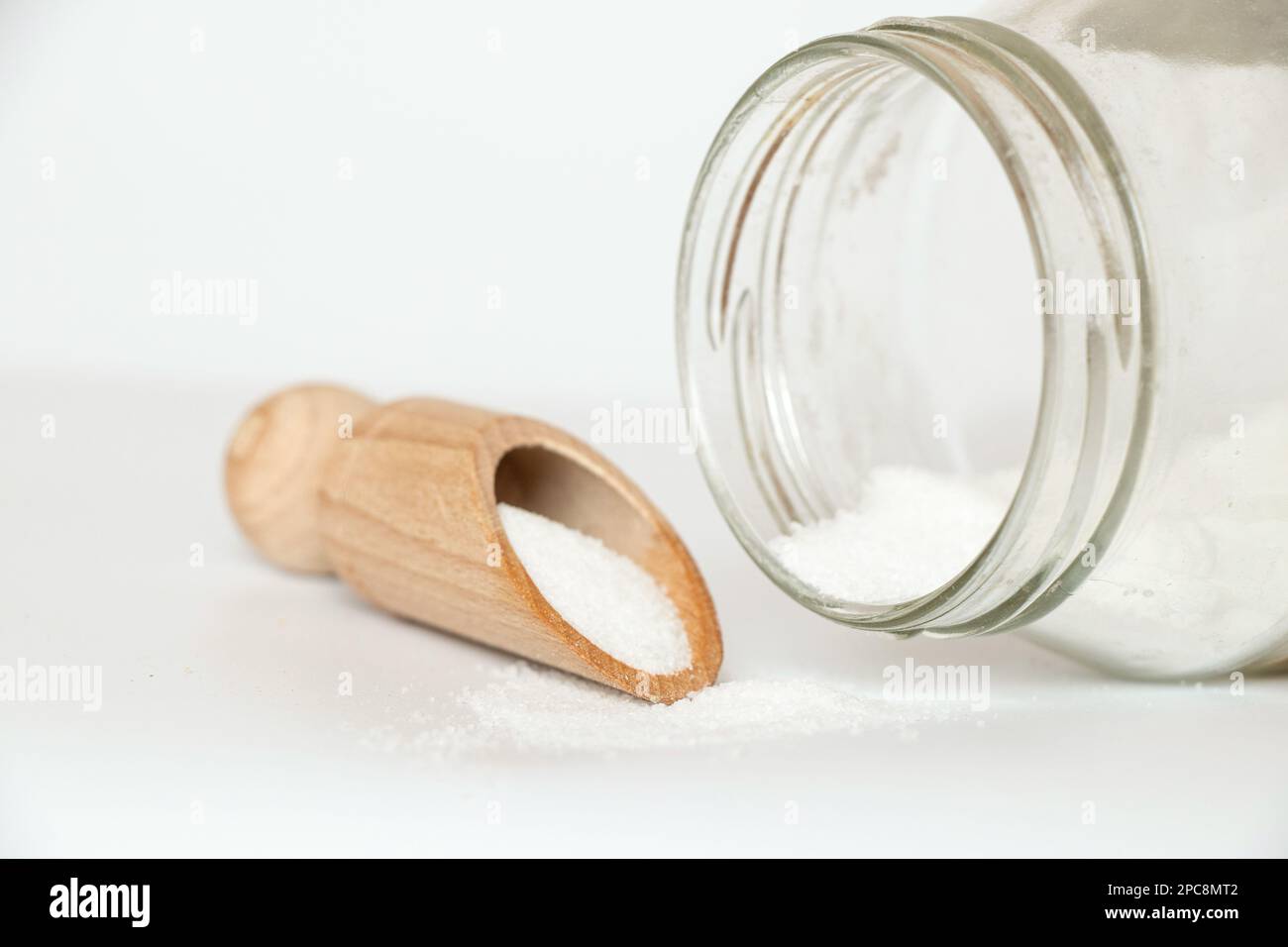 Edible salt in a wooden spoon and a glass jar next to it on a white ...