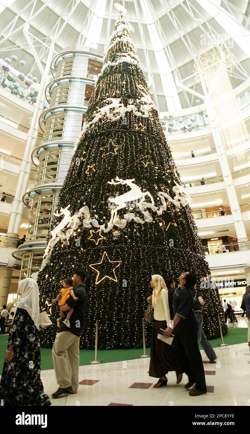 Malaysian shoppers walk past a five story high Christmas tree displayed ...