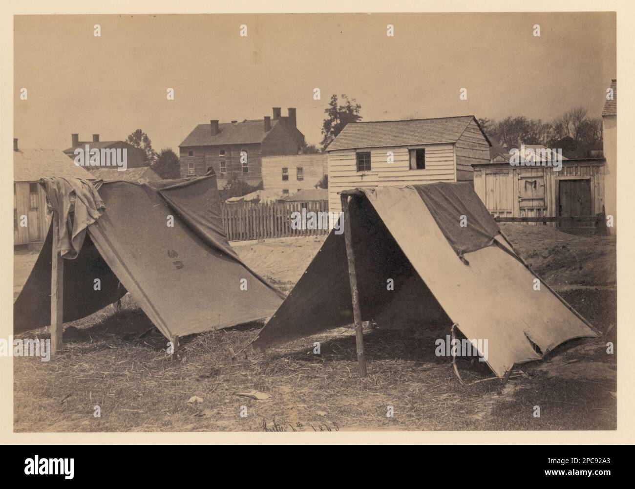 Two small tents, with wood frame buildings in the background. Title ...