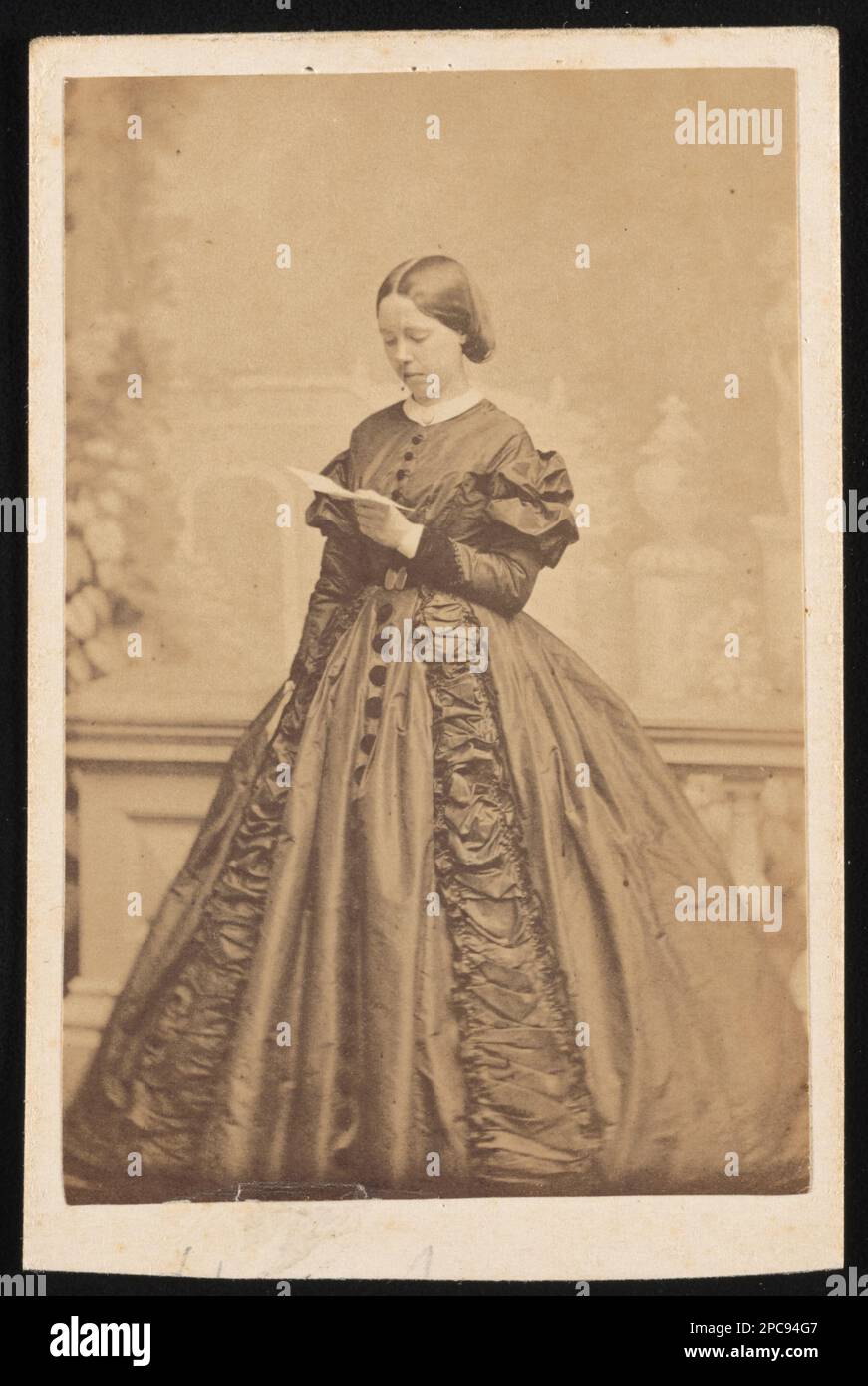 Miss Head reading a letter in front of painted backdrop showing a ...