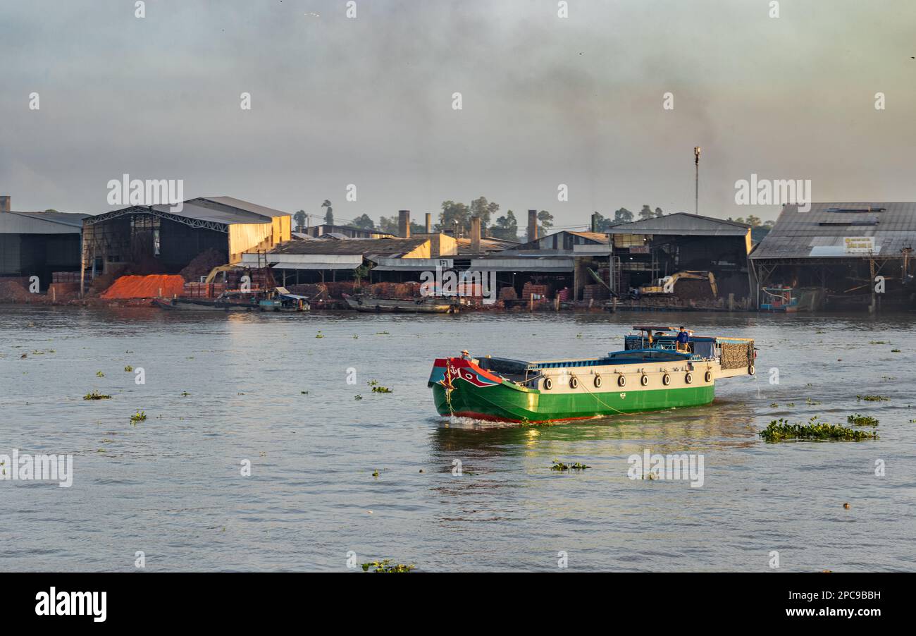 A motorised barge moves out into the Mekong River next to warehouses ...