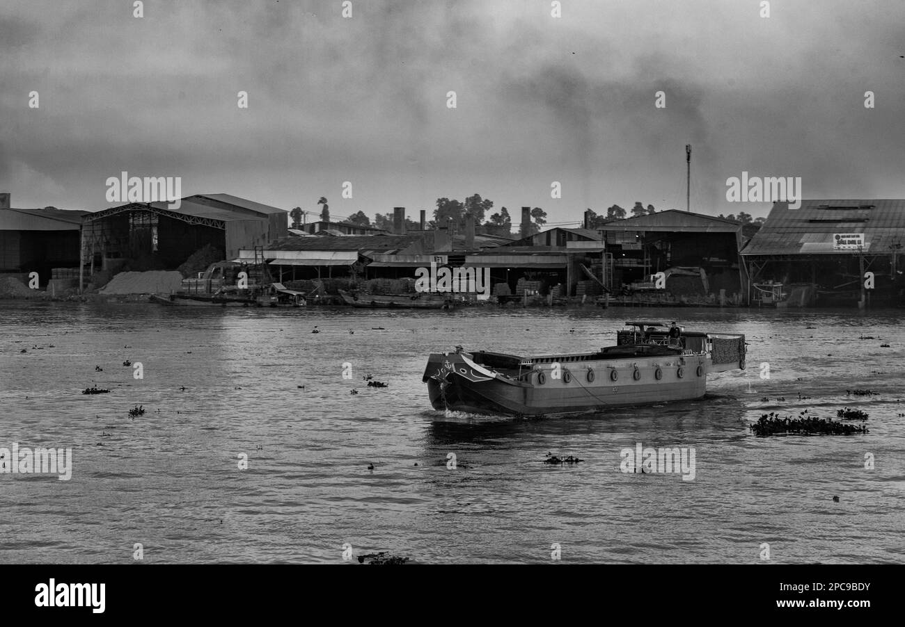 A motorised barge moves out into the Mekong River next to warehouses ...