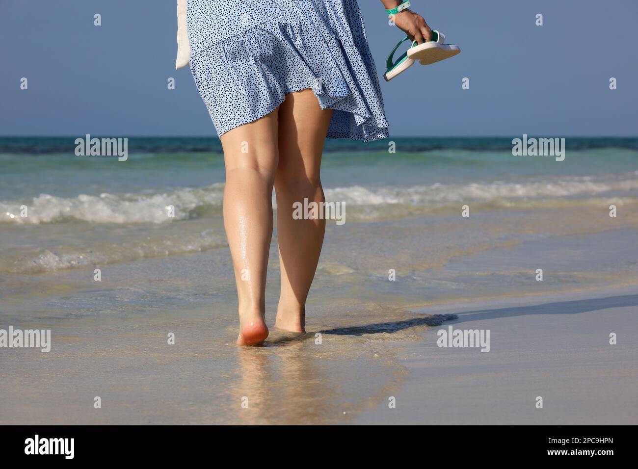 Barefoot woman in summer dress walking by the sand with removed flip ...