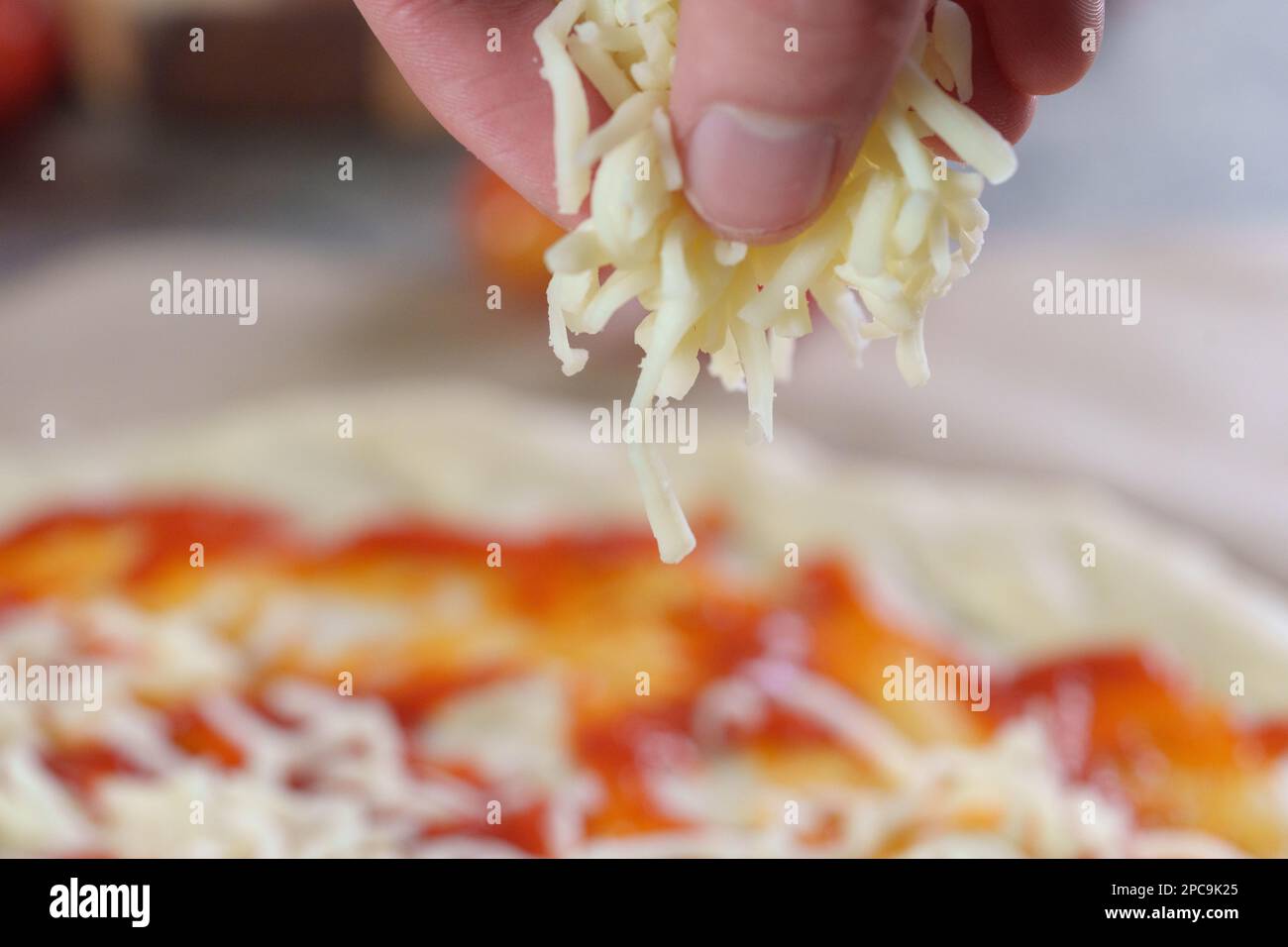 A person's hand adding grated cheese to pizza, process of making pizza ...