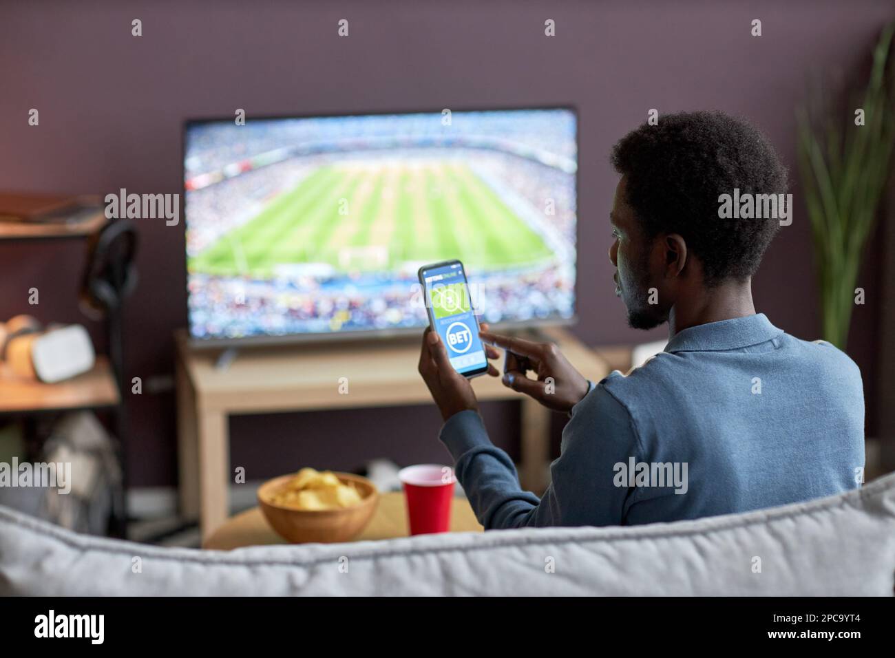 Back view of man holding smartphone with sports bets app on screen ...