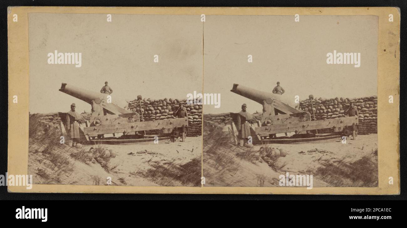 Three soldiers posing by a mounted cannon with a wall of sandbags ...